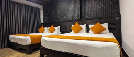 Quarto de hotel com duas camas, cada uma com roupa de cama branca e detalhes em laranja. O quarto possui uma cabeceira de madeira escura e uma parede estampada.