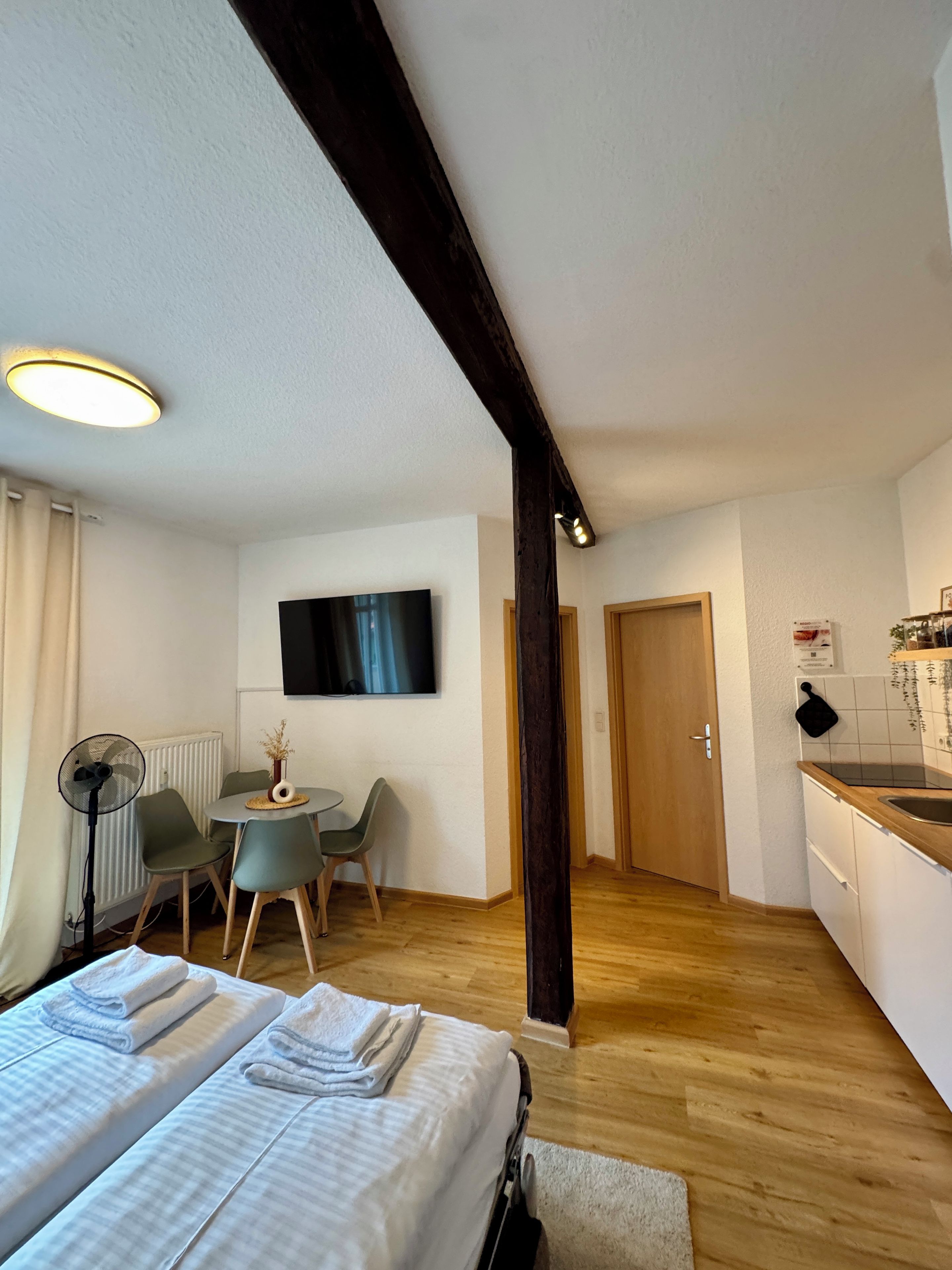 Quarto de hotel com cama, escrivaninha, cadeira, televisão e cozinha compacta.