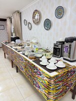 Disposição de buffet com diversos alimentos, uma cafeteira e pratos decorativos na parede.
