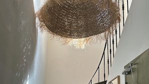 Uma escadaria com corrimão em ferro forjado, um pendente decorativo de fibra e um vaso de planta na base.