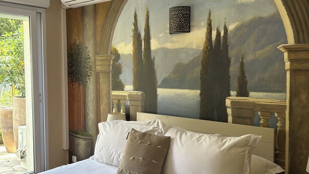 Um quarto com uma cama grande, uma janela e um mural com árvores e montanhas na parede.