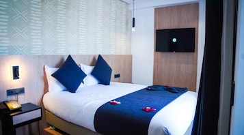Quarto de hotel com uma cama, mesa de cabeceira com telefone, televisão na parede e papel de parede estampado.
