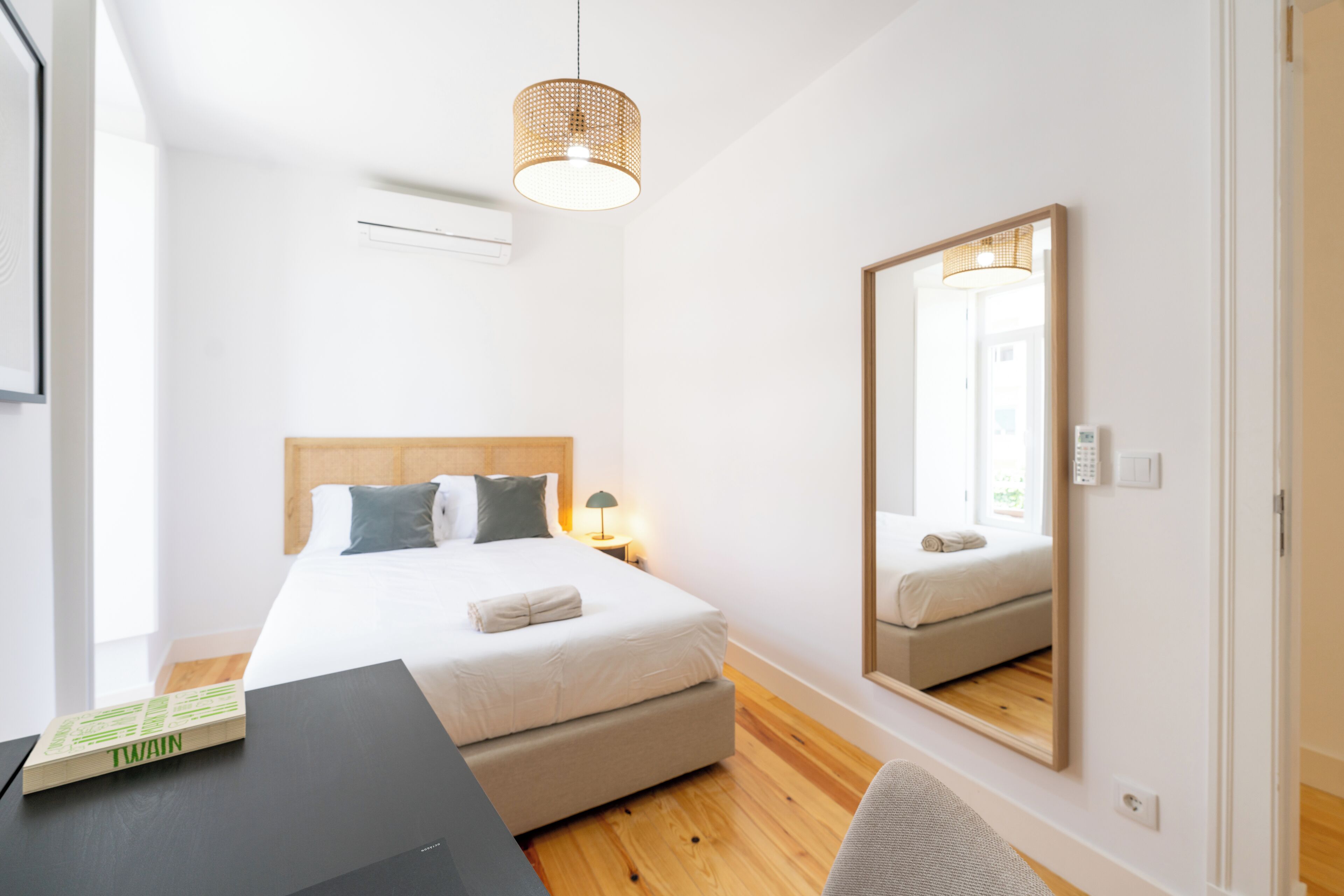 Quarto de hotel moderno com cama, mesa de cabeceira e um espelho grande.