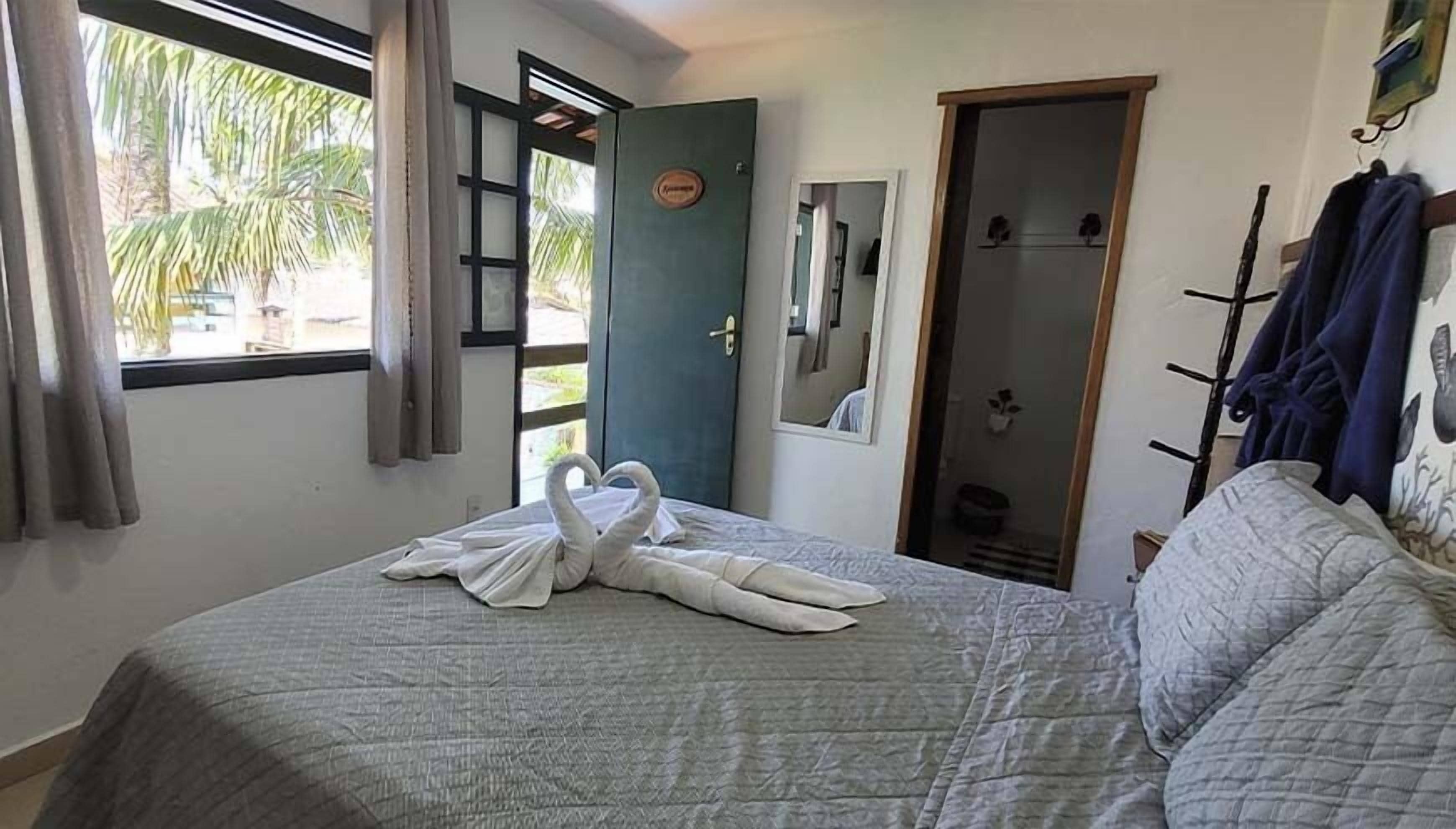 Um quarto com cama, porta, espelho e janela com cortinas.