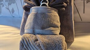 Toalha dobrada com uma etiqueta de metal sobre uma cama com almofadas estampadas com flores.