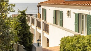 Um edifício costeiro com telhado ladrilhado, persianas verdes e vista para o mar.