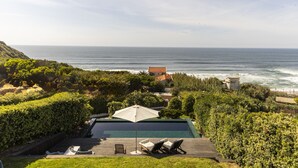 Piscina privativa com espreguiçadeiras e guarda-sol, cercada por vegetação exuberante e vista para o oceano.