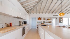 Cozinha moderna com armários brancos, teto de madeira e uma ilha central com pia.