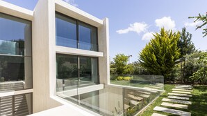 Um edifício moderno com grandes janelas de vidro e guarda-corpo de vidro, com vista para um jardim com pedras para caminhos.