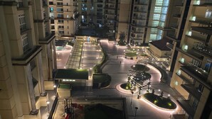 Um edifício residencial alto com várias varandas, um pátio central com escada em espiral e uma rua bem iluminada.