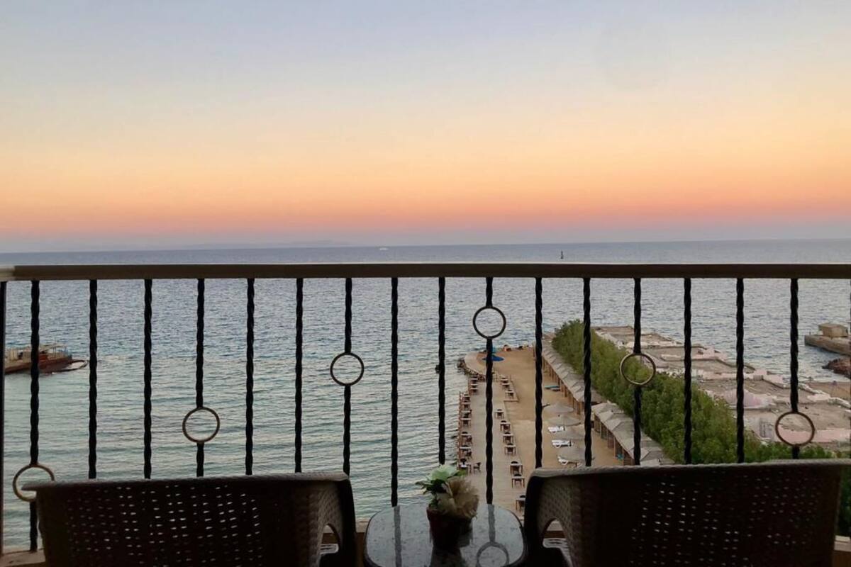 Varanda com vista para o mar, área de estar e costa distante com edifícios e praia.