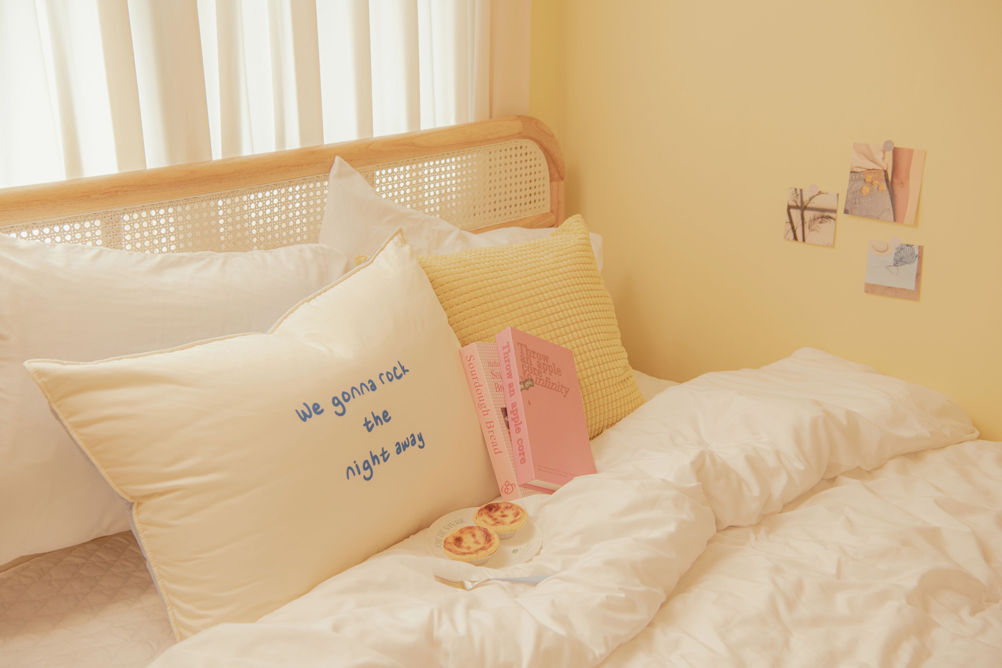 Cama bem arrumada com travesseiros, um livro e um prato com comida.