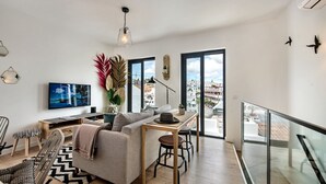 Uma sala de estar moderna com sofá, mesa de jantar e televisão. Há janelas amplas e uma varanda.