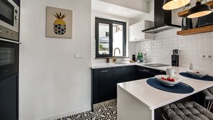 Cozinha moderna com armários escuros, bancadas brancas e uma ilha central. Há uma janela com vista para o exterior, e uma obra de arte com tema de abacaxi na parede.