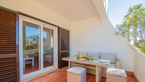 Varanda com porta de vidro, móveis de vime e uma mesa posta com pratos e bebidas.