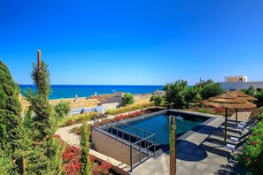Área da piscina com vista para o mar, cercada por vegetação e um pequeno gazebo.