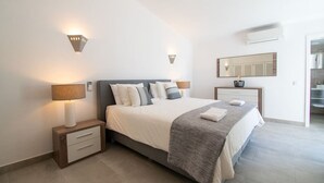 Quarto moderno com cama, mesas de cabeceira, um espelho e ar condicionado.