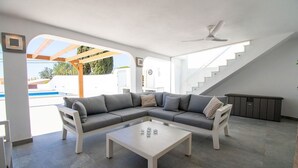 Uma sala de estar moderna com um sofá modular cinza, uma mesa de centro branca e uma escada que leva a um andar superior.