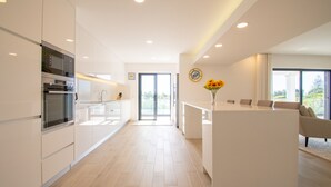 Uma cozinha moderna com eletrodomésticos embutidos, uma área de refeições com ilha central e vista pela porta de vidro.