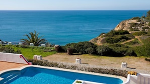 Piscina com vista para o mar, cercada por vegetação e um caminho de pedra.