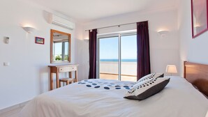 Quarto de hotel com cama, escrivaninha, cadeira, espelho e vista para o mar.