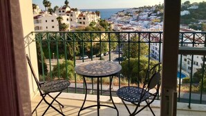 Uma varanda com vista para uma cidade costeira, com uma mesa redonda e duas cadeiras.