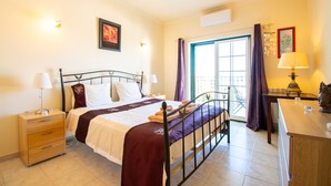 Quarto de hotel com cama, mesas de cabeceira, escrivaninha e janela com cortinas.
