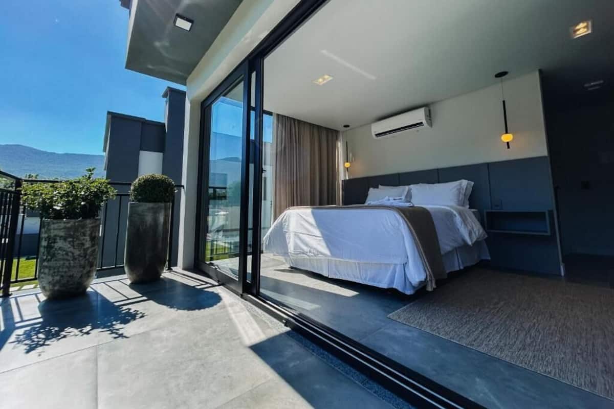 Quarto moderno com cama grande, porta de vidro para uma varanda e vista para o exterior.