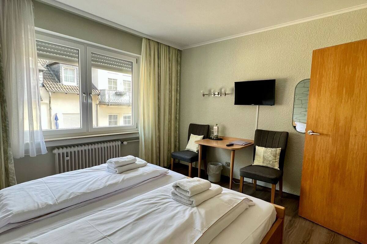 Quarto de hotel com cama grande, escrivaninha, cadeira, televisão fixada na parede e guarda-roupa.