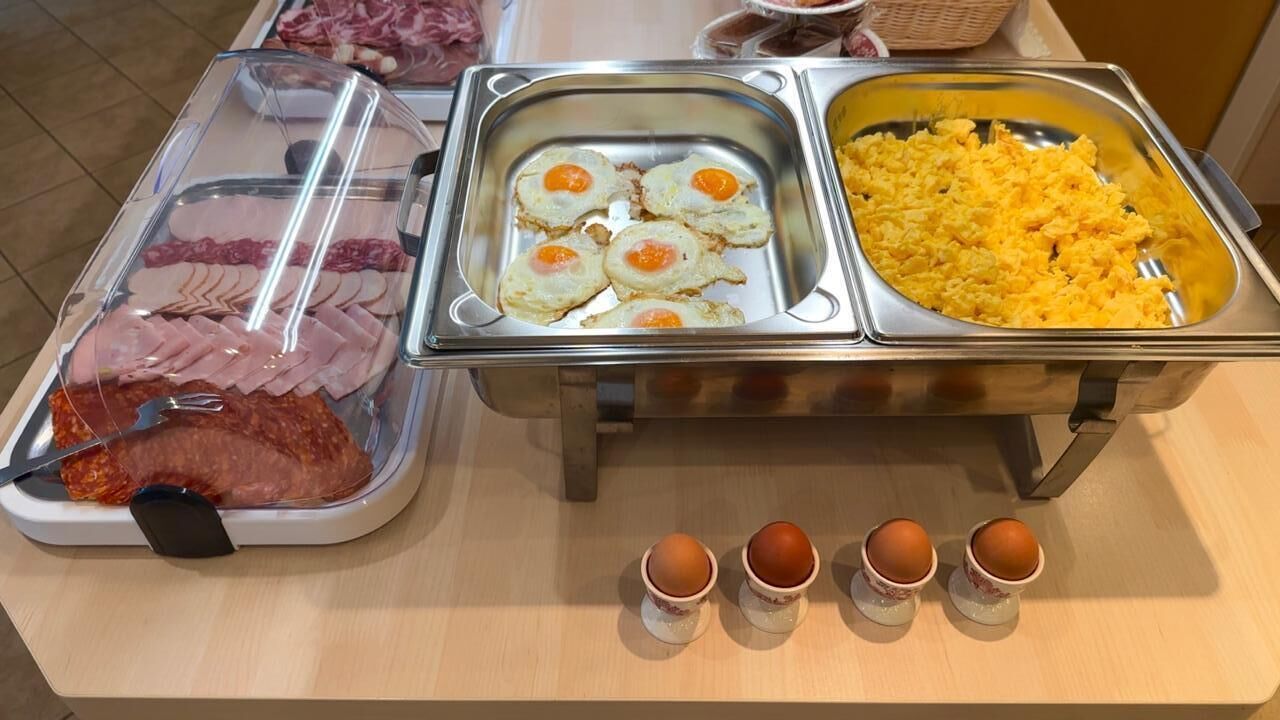 Buffet com diversas opções de comida, incluindo carnes fatiadas, ovos fritos e mexidos.