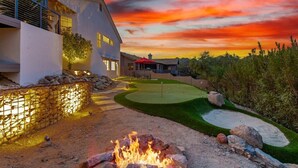 Uma casa moderna com um jardim bem cuidado, um espaço para fogueira e um campo de prática de golfe.