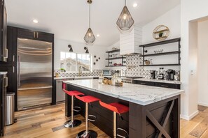 Cozinha moderna com uma ilha grande, eletrodomésticos de aço inoxidável e banquetas vermelhas.