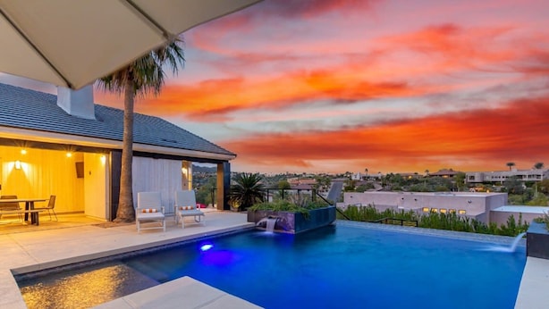 Piscina com cachoeira, varanda coberta com assentos e vista para o pôr do sol.