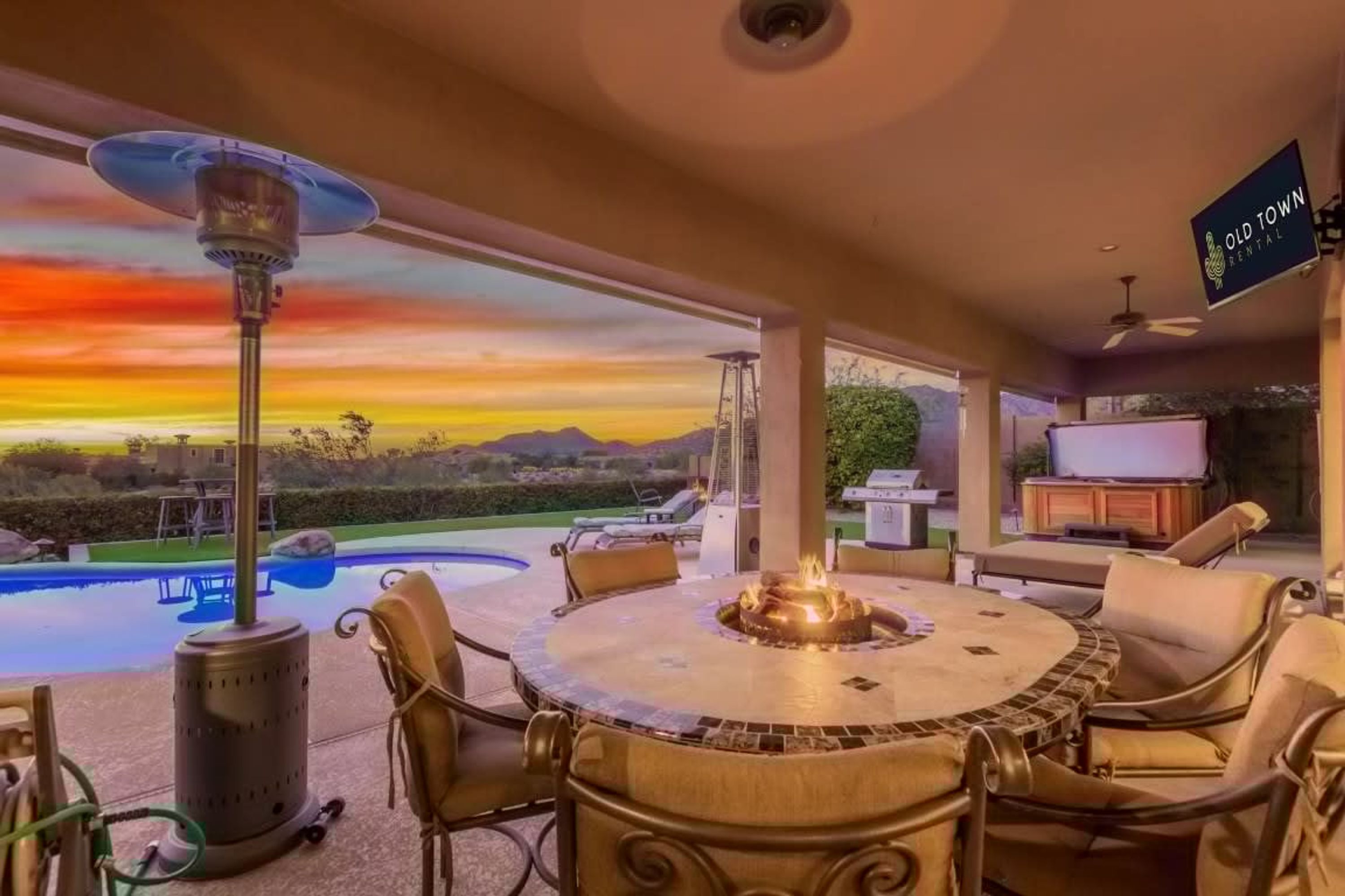 Um pátio com uma mesa redonda, cadeiras, lareira e vista para uma piscina e montanhas.