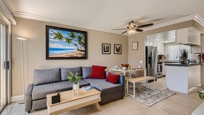 Uma sala de estar moderna com um sofá cinzento, almofadas vermelhas, uma mesa de centro de madeira e uma pintura de uma cena de praia.