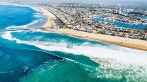 Vista aérea de uma cidade costeira com praia, marina e edifícios bem próximos.