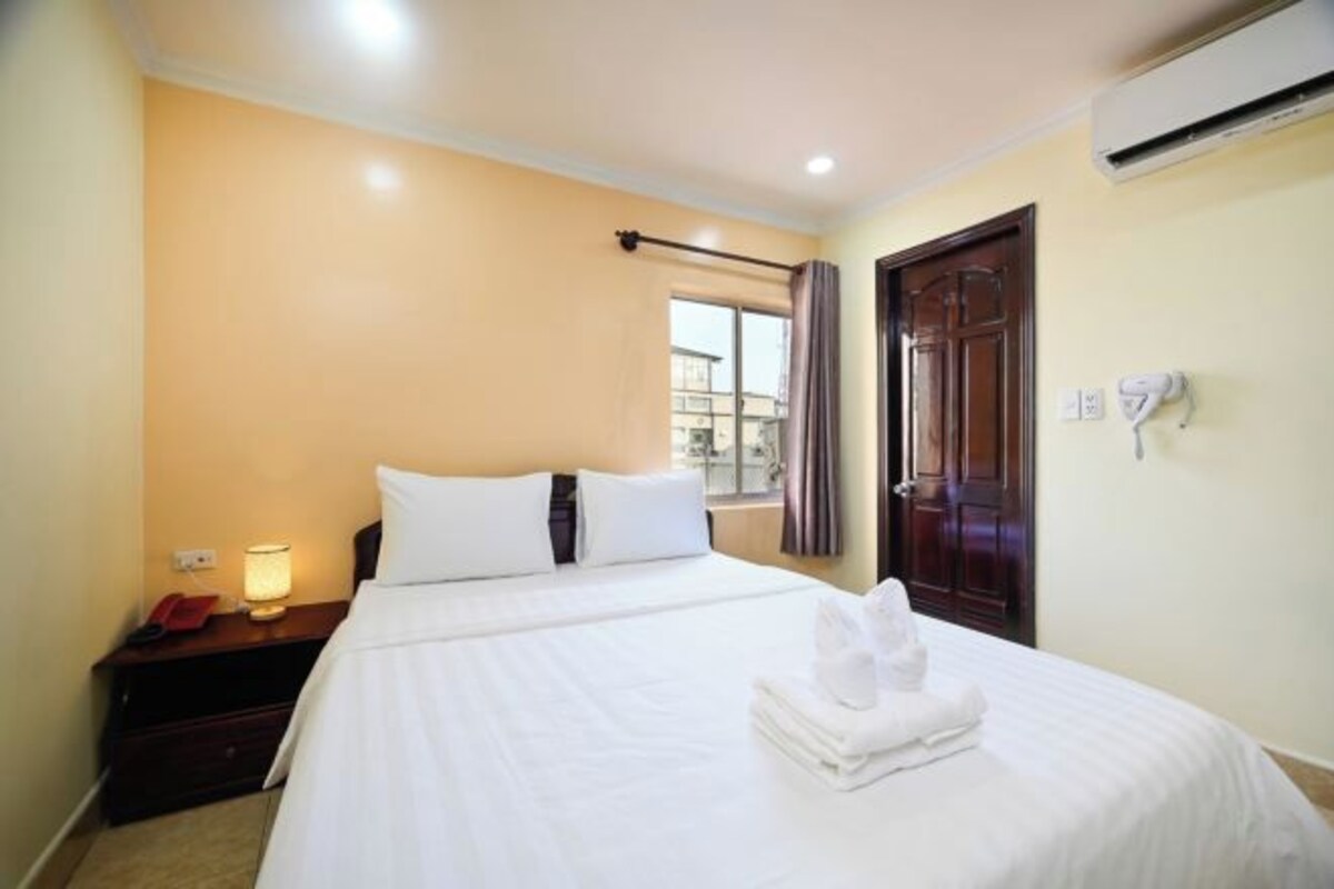 Quarto de hotel com uma cama grande, luminária de cabeceira, janela com cortinas e ar condicionado.