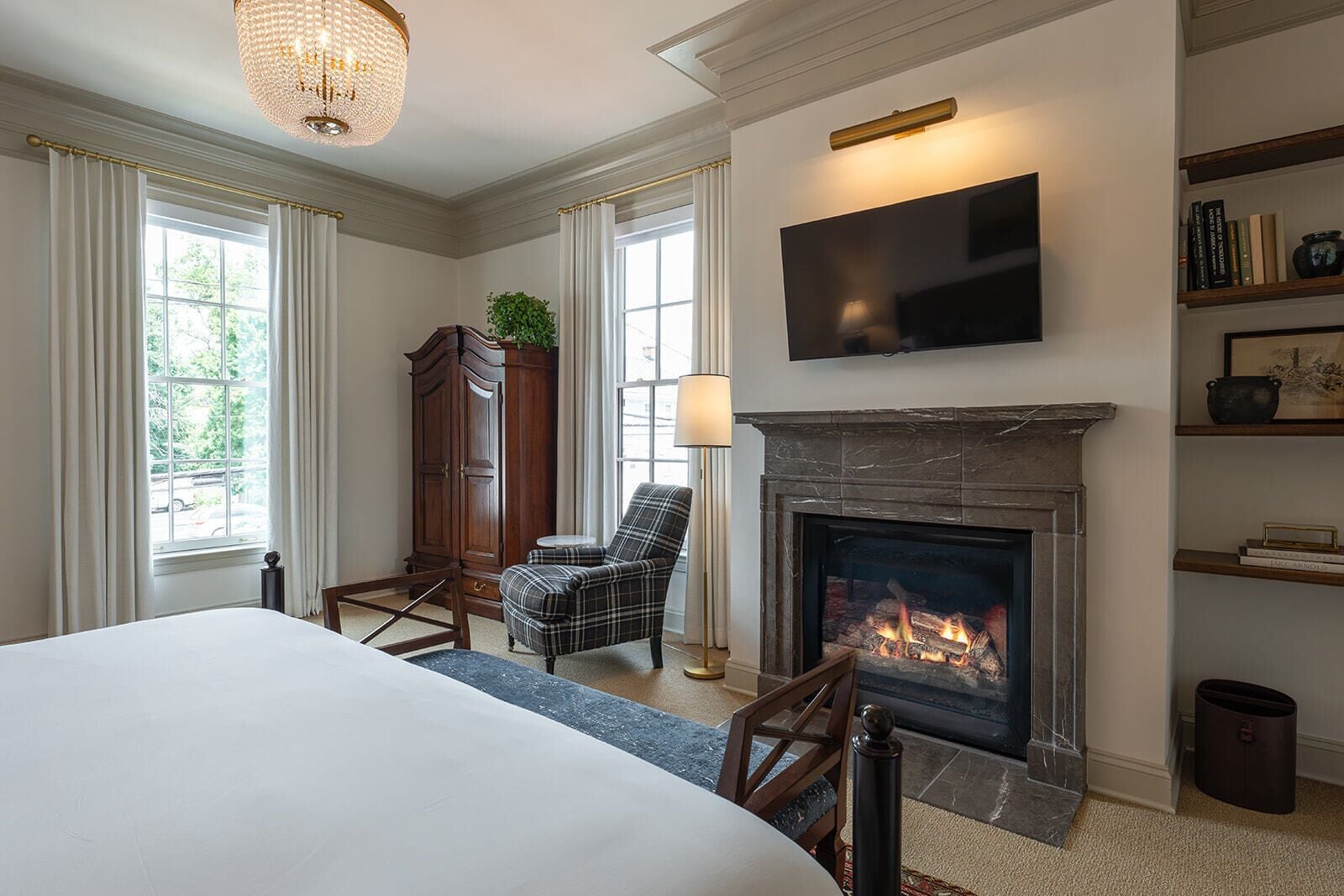 Quarto de hotel com uma cama grande, lareira, televisão na parede e vista para o exterior pelas janelas.