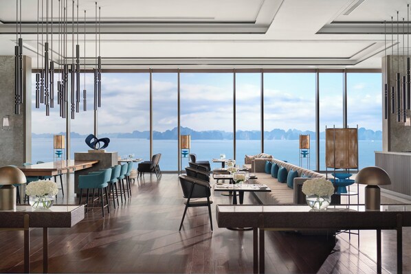Uma sala de jantar moderna com vista para o mar, com uma mesa comprida, cadeiras e um bar.