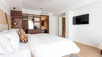 Quarto de hotel moderno com uma cama grande, cabeceira de madeira, televisão fixada na parede e banheiro visível através de uma porta aberta.