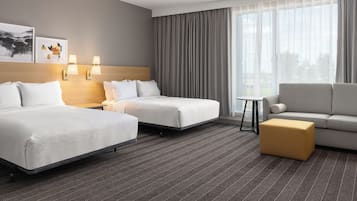 Quarto de hotel com duas camas, um sofá, uma mesa pequena e uma janela grande com cortinas.