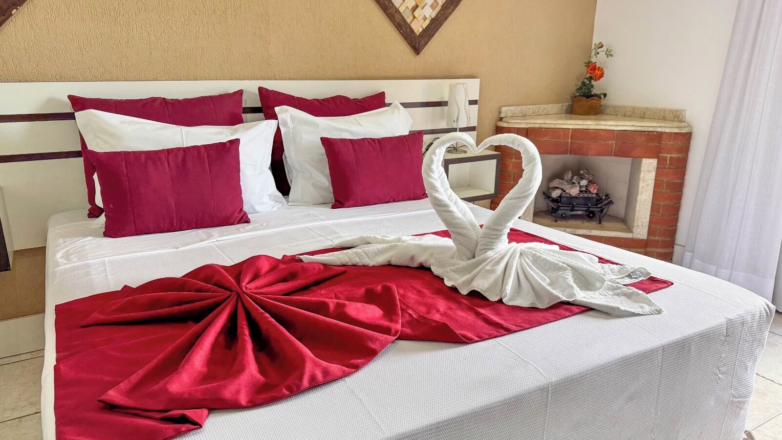 Cama bem arrumada com manta vermelha e dois travesseiros em forma de cisne branco.