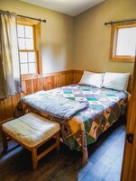 Quarto com cama de madeira, um banquinho e uma janela.