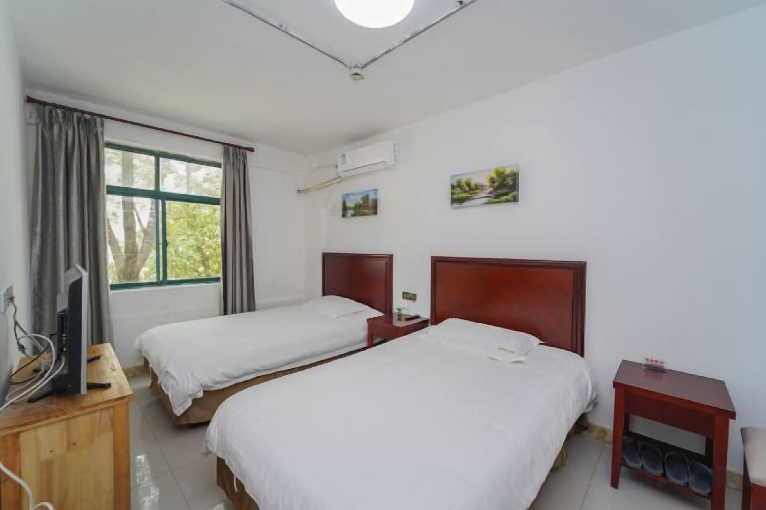 Quarto de hotel com duas camas, cómoda de madeira, televisão e janela com cortinas.