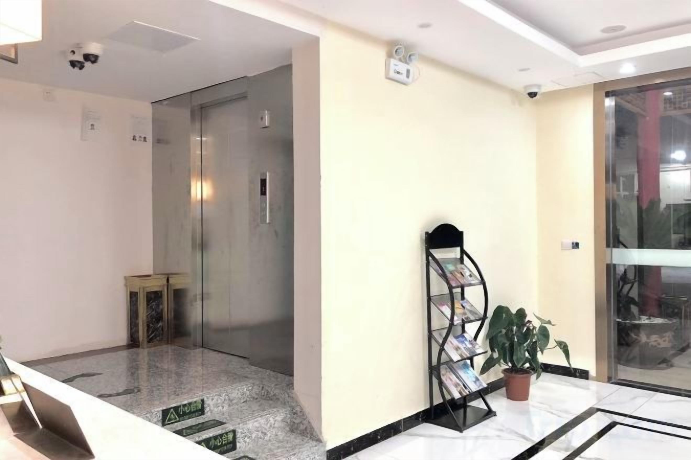 Um saguão de hotel com uma mesa de recepção, um elevador de vidro e um vaso de plantas.