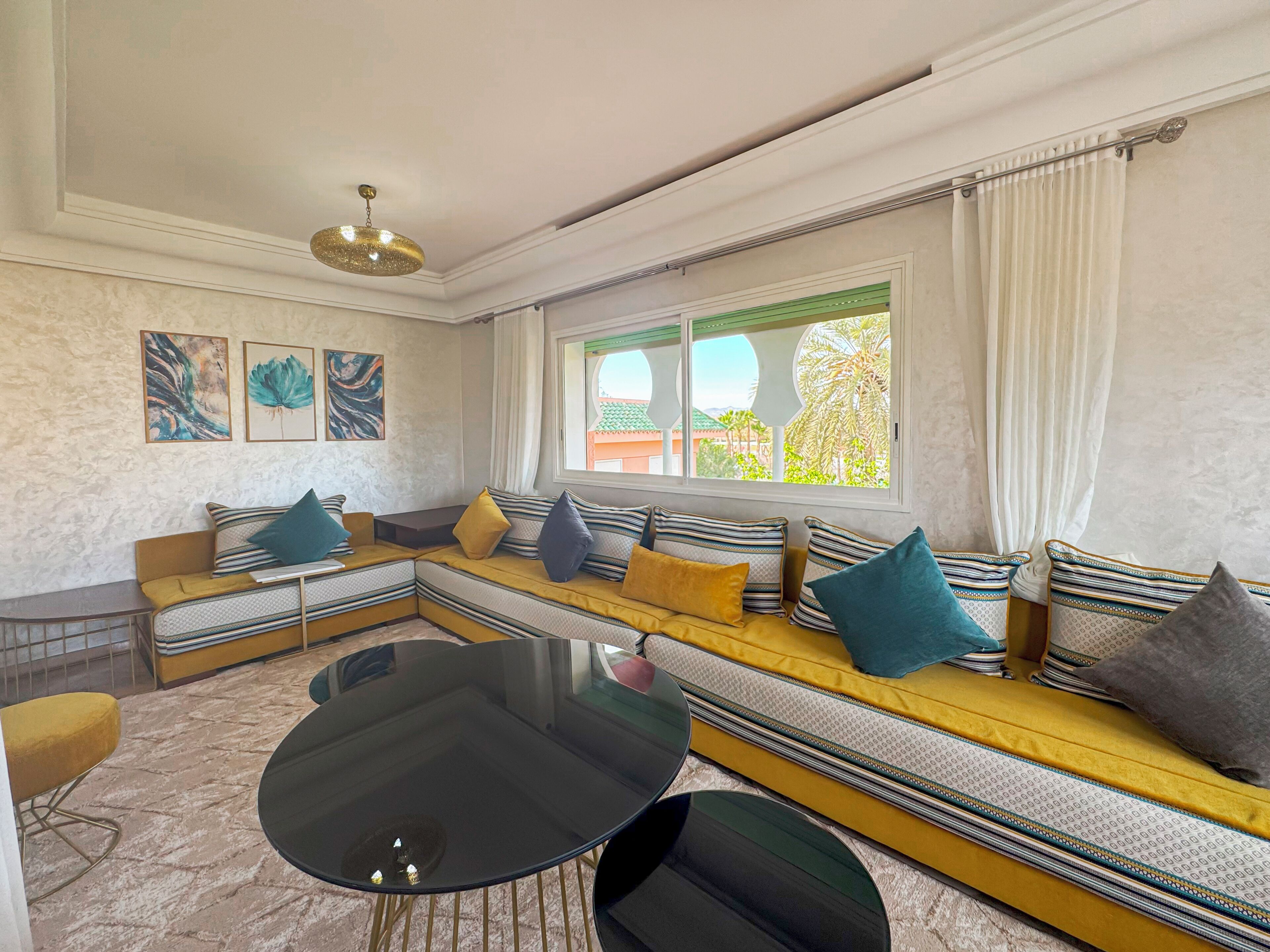 Uma sala de estar moderna com um sofá seccional, uma mesa de centro de vidro e vista para o exterior através de grandes janelas.