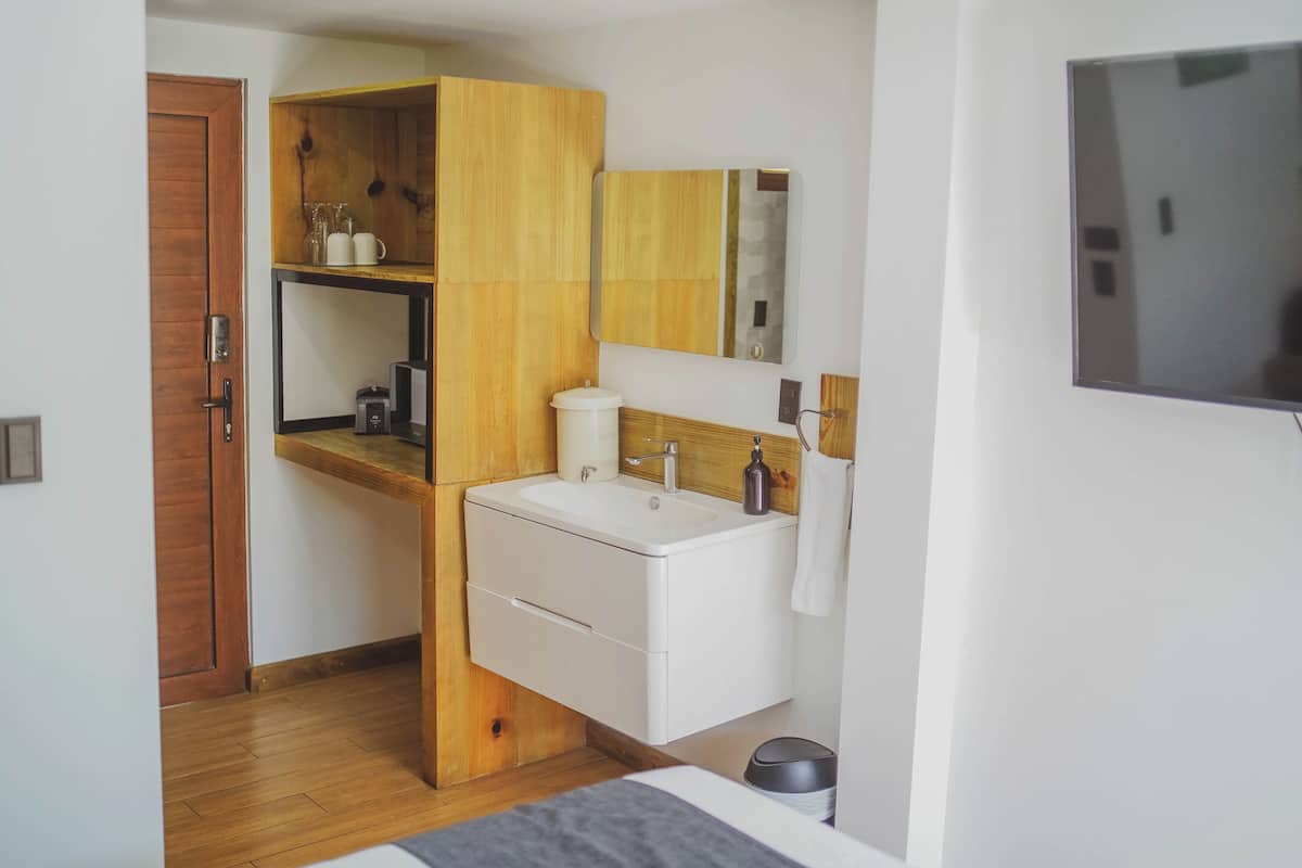 Casa de banho compacta com toucador de madeira, lavatório branco, espelho e sanita.