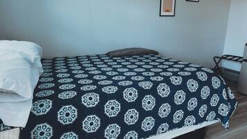 Uma cama bem arrumada com colcha estampada, uma mesa de cabeceira com abajur e uma parede com duas quadros.