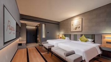 Quarto de hotel com duas camas, um banco, televisão presa na parede e corredor que leva a outro quarto.