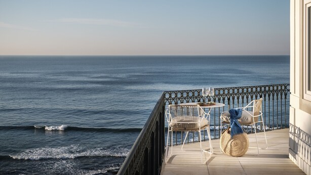 Varanda com vista para o mar, com duas cadeiras e uma mesa.
